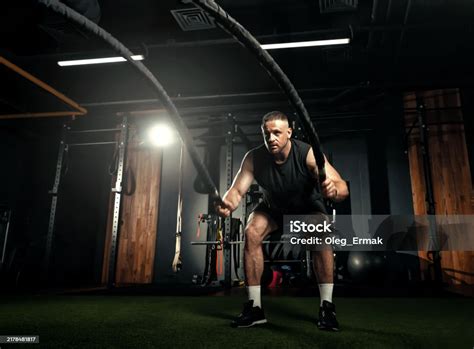 보디 빌더는 체육관 홀에서 근육 피트니스를위한 배틀 로프와 종사하고 있습니다 근력을 위한 격렬한 운동으로 훈련과 지구력 텍스트를 위한 공간 35 39세에 대한 스톡 사진 및