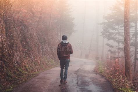 Man Walking Alone On A Road Through A Dark Foggy Forest Stock Image