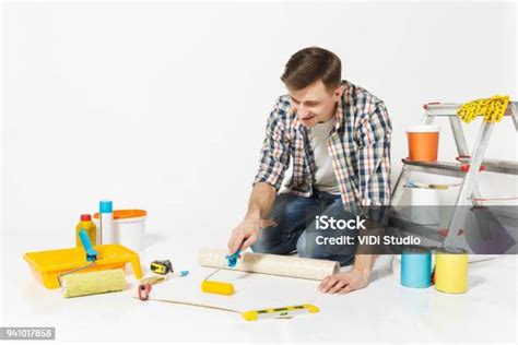 젊은 남자 벽지 롤 페인트 롤러 흰색 배경에 고립 된 재건축 아파트 룸에 대 한 악기와 함께 바닥에 앉아 벽지 액세서리를 붙이기 그림 도구 수리 홈 개념 개선에 대한 스톡