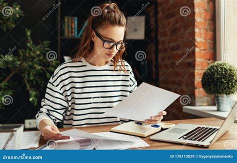 Young Dedicated Woman Revising Papers While Working On Project At