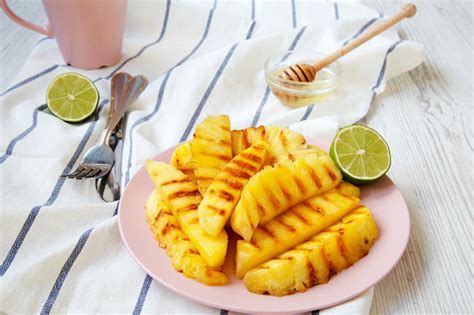 흰색 나무 표면 측면 보기 석 회와 꿀 핑크 접시에 파인애플 쐐기를 구이 여름 음식입니다 간식에 대 한 아이디어입니다 근접 촬영입니다 건강한 생활방식에 대한 스톡 사진 및