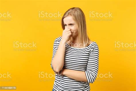 스튜디오에서 노란 오렌지 배경에 고립 된 손으로 코를 덮고 줄무늬 옷에 자극 된 혐오 젊은 여자의 초상화 사람들은 진심으로 감정 라이프 스타일 개념입니다 복사 공간을 모의