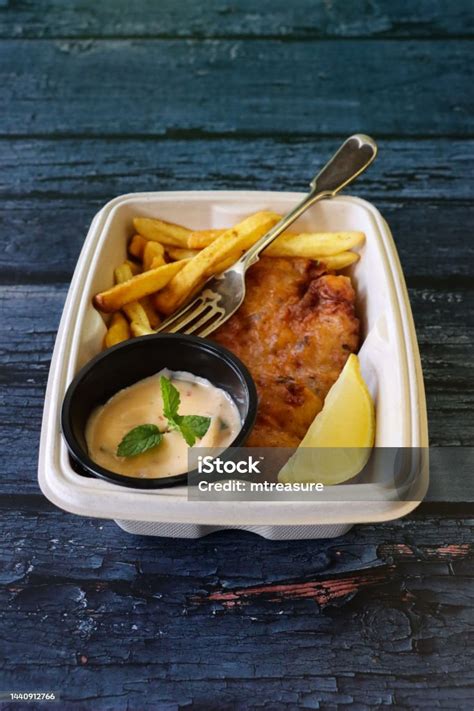 일회용 판지 테이크아웃 상자에 담긴 피쉬 앤 칩스 이미지 레몬 슬라이스 타르타르 소스의 플라스틱 그릇 포크 파란색 나뭇결 배경