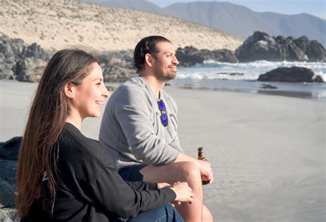 Joven Pareja Latina Sentada En La Playa Compartiendo Y Mirando El Horizonte Feliz Foto Premium
