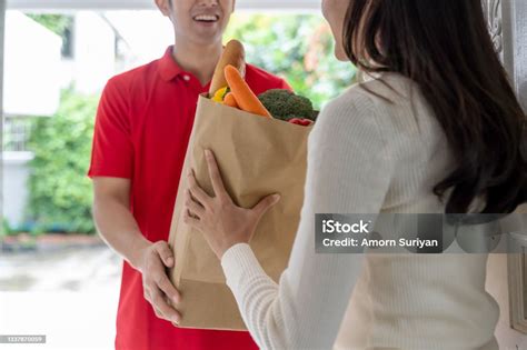 종이 봉투나 종이 통으로 신선한 음식을 받는 여성은 문 앞에서 배달원으로부터 배달원으로부터 우편 배달 음식 집에서 받는 사람에게