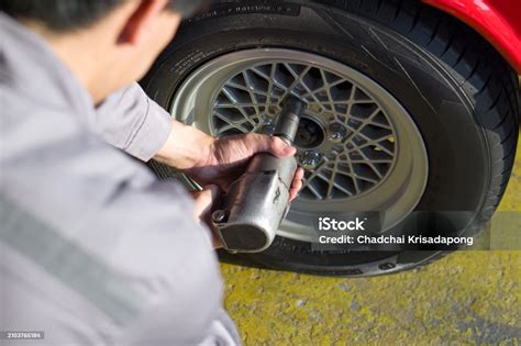 제복을 입은 정비사가 공압 임팩트 렌치를 사용하여 자동차 바퀴에서 작업하며 타이어를 교체하거나 바퀴 또는 타이어와 관련된 유지 보수를 수행하는 과정에서 작업합니다 뒤로