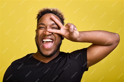 쾌활하게 웃는 흑인 남자는 평화의 상징을 보여줍니다 프리미엄 사진