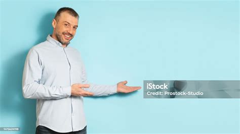 캐주얼한 행복한 잘생긴 중년 남자가 여유 공간을 보여주고 파란색 스튜디오 배경에 무언가를 광고합니다 40 44세에 대한 스톡 사진 및 기타 이미지 Istock