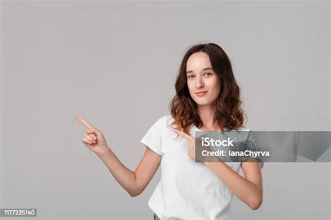 회색 배경 위에 고립 된 프레임의 왼쪽에있는 빈 공간을 가리키는 흰색 티에 예쁜 갈색 머리 여자 광고 의 공간을 복사합니다 여자에 대한 스톡 사진 및 기타 이미지 Istock