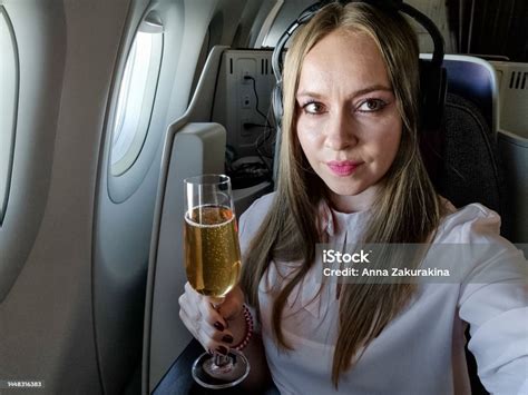 공식 옷을 입은 여자는 헤드폰을 착용하고 사업가는 항공기에서 비즈니스 프리미엄 클래스에 앉아 있고 숙녀는 샴페인 음료 한 잔을 들고 마시고 비행기를 타고 럭셔리 여행을