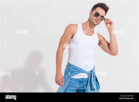 Portrait Of Young Man In Undershirt Fixing His Sunglasses While Standing On White Background And