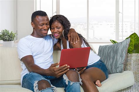 노트북 컴퓨터와 재미 인터넷 네트워킹 함께 현대 아파트에서 거실 소파 소파에서 즐기는 사랑 하는 젊은 행복 하 고 아름 다운 검은 아프리카계 미국인 부부에 2명에 대한 스톡