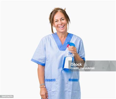 중간 나이 갈색 머리 청소기 여자 서 치아를 보여주는 자신감 미소로 웃 고 행복 한 얼굴로 고립 된 배경 위에 가사 유니폼을 입고 가사 집안일에 대한 스톡 사진 및 기타