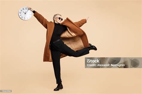 금발 짧은 머리와 코트와 선글라스 춤을 입고 젊은 소식통 여자 웃는 베이 지 배경 위에 고립 된 시계 가을에 대한 스톡 사진 및