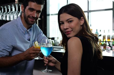 잘 생긴 남자와 아름다운 여자의 커플이 럭셔리 바에서 만나 칵테일을 마시고 옥상 레스토랑 바에서 밤 파티를 축하하는 음료와 함께 즐기는 사람들 2명에 대한 스톡 사진 및