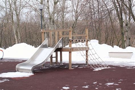 겨울에는 놀이터 슬라이드와 등반 그물 눈 덮개가 있는 빈 놀이터 장비 금속 슬라이드 및 로프 네트 활주와 그물을 가진 나무로 되는 놀이 구조 부분적으로 눈 속에 있는 어린이