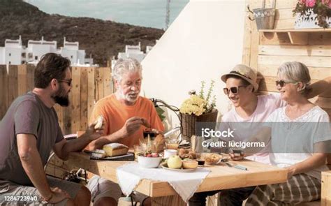 일광욕 아래 테라스에서 함께 아침 식사를하는 가족 그룹 음식과 음료의 구색나무 테이블에 앉아 십대에서 조부모에 미소 사람들의 4 세대 초콜릿에 대한 스톡 사진 및 기타