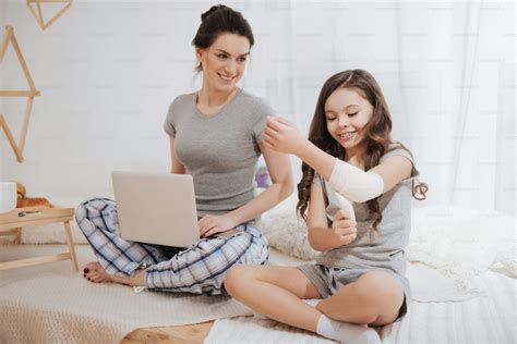 가족 유용한 주말을 즐기십시오 긍정적 인 세련된 젊은 여성이 집에 앉아 노트북을 사용하는 동안 딸이 팔꿈치에 붕대를 감고 약을 배우고 있다 사진 Unsplash의 기술 이미지