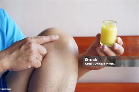 클로즈업 손은 무릎에 바르기 위해 허브 옐로우 밤 병을 들고 있습니다 개념 건강 관리 구급 집에서 자기 관리 통증 부상 염좌를 완화하기 위해 허브 연고를 사용하십시오 무릎에