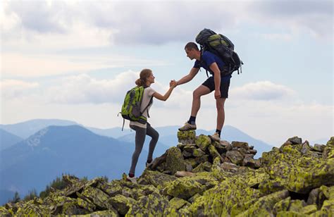 배낭을 가진 젊은 관광객 운동 소년은 밝은 여름 하늘과 산맥 배경에 대한 클라임 바위 산 꼭대기에 슬림 소녀를하는 데 도움이됩니다 관광 여행 및 건강한 라이프 스타일 개념