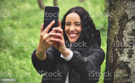 하이킹 을하는 동안 숲에 홀로 서서 휴대 전화로 셀카를 찍는 매력적인 젊은 여성의 샷 20 29세에 대한 스톡 사진 및 기타