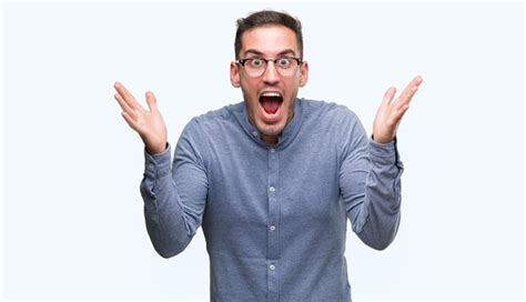 우아한 잘생긴 젊은 남자 미친을 축 하 하는 안경을 착용 하 고 무기와 성공을 위한 놀 제기 및 오픈 눈 비명 흥분 우승자 개념 긍정적인 감정 표현에 대한 스톡 사진 및