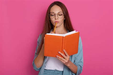 사려 깊은 표정으로 매력적인 여성의 수평 초상화 그녀의 작업에 대해 생각 뭔가를 계획 정장과 안경을 입고 핑크 스튜디오 배경