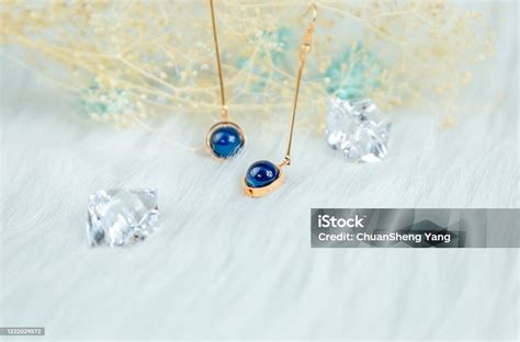 파란색 둥근 구슬과 황금 색 노란색 금속으로 만든 귀걸이 배경으로 노란색 건조 잔디 식물 흰색 봉제 천과 투명 한 얼음 장식품 0명에 대한 스톡 사진 및 기타 이미지