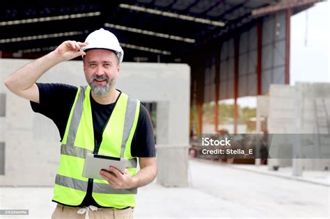 건설 현장에서 디지털 태블릿을 들고 안전 조끼와 헬멧을 쓴 행복한 미소 짓는 선임 작업자 엔지니어 감독의 초상화 건설 현장
