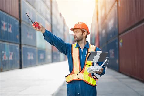 남성 컨테이너 야드 작업자는 상업용 부두 현장의 화물 화물선에서 디지털 태블릿으로 컨테이너 상자를 적재하는 것을 제어합니다 컨테이너 박스 화물 화물선에서 운송 또는 배송