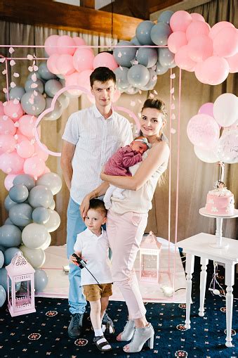 젊은 부모의 초상화는 공기 풍선 핑크 회색 배경에 생일 휴가 파티를 축하 아이 아이 아기 소녀를 포옹 팔에 유지합니다 행복한 가족 어머니 아버지 딸 아들 아기에 대한 스톡
