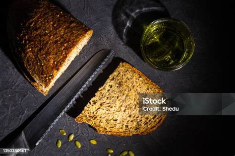 아마 양귀비 씨앗 참깨 기장 호박 해바라기 씨 유리 항아리에 올리브 오일 검은 색 배경 하드 라이트 낮은 키에 사진 칼과 소박한 천연 효모가없는 빵 조각 갈색에 대한 스톡
