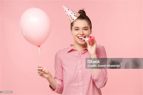 컬러 안경과 생일 모자를 쓴 행복한 소녀 휘파람 불기 분홍색 풍선 들고 웃고 파티를 즐기고 분홍색 배경에 고립 되어 있습니다 생일에 대한 스톡 사진 및 기타 이미지 Istock