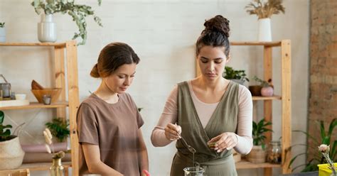 두 명의 젊은 여성 중 한 명이 천연 수제 화장품을 위한 혼합물을 만드는 동안 분쇄 비누 덩어리로 유리 그릇에 에센스 오일을 넣고 있습니다 사진 Unsplash의 행복 이미지