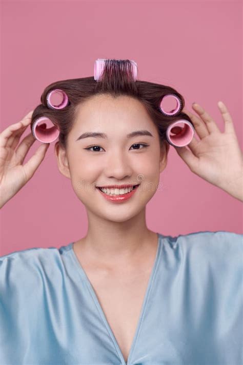 Housewife Applies Hair Curlers Dressed In Casual Robe Poses Against Rosy Background Stock