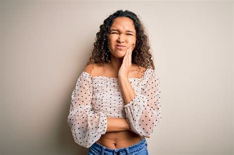 치통이나 치아질환으로 인해 고통스러운 표정으로 입을 만지는 흰색 배경 위에 서있는 캐주얼 한 티셔츠를 입은 곱슬 머리를 가진 젊은 아름다운 여성 치과 의사 T 셔츠에 대한