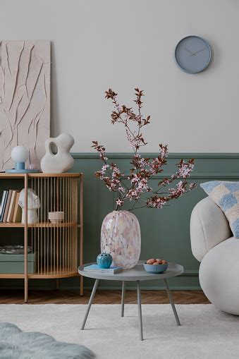 모형 포스터 프레임 Boucle 소파 둥근 커피 테이블 꽃이 만발한 가지가 있는 유리 꽃병 베이지색 카펫 및 개인 액세서리가 있는 거실 인테리어의 봄 구성 가정 장식 템플렛