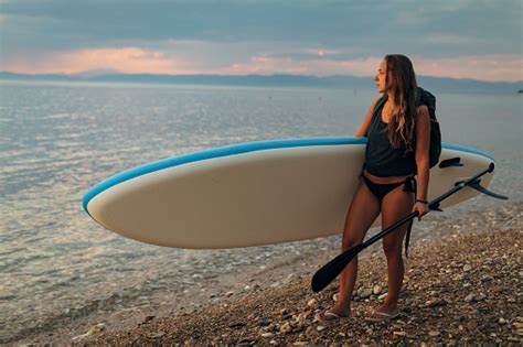 한 여성이 Sup 보드를 들고 해변을 따라 걷는 동안 아름답고 잔잔한 바다를 감탄스럽게 바라 봅니다 여자에 대한 스톡 사진 및 기타 이미지 Istock
