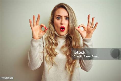 겨울 터틀넥 스웨터를 입은 아름다운 여성은 손가락으로 확인 승인 기호를하고 놀랍고 충격을 받은 흰색 배경 위에 있습니다 미친 표현 Omg에 대한 스톡 사진 및 기타 이미지
