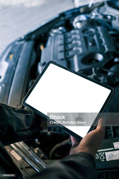 정비사가 자동차 엔진 위에 들고 있는 빈 화면이 있는 태블릿으로 차량 유지 보수 및 수리를 위한 최신 진단 도구를 상징합니다 엔진이 배경에서 보입니다 건강 진단에 대한 스톡