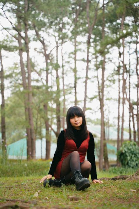 숲 속에 앉아 있는 빨간 드레스를 입은 젊은 여성 · 무료 스톡 사진