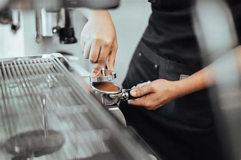 탬퍼를 사용하여 분쇄 커피를 포터필터에 밀어 넣는 바리스타 바리스타가 커피 머신으로 커피를 만드는 모습을 가까이서 볼 수