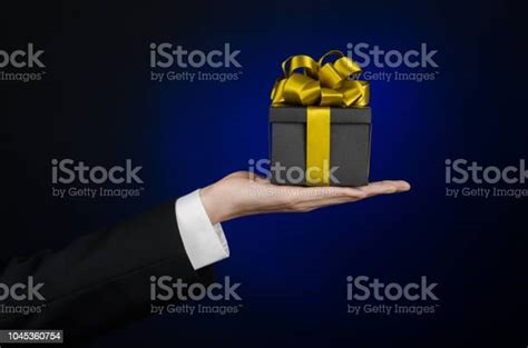 축 하와 선물의 테마 절연 스튜디오에 진한 파란색 배경에 골드 리본 아름 다운 블랙 박스에 포장 하는 독점적인 선물 비싼 선물을 들고 검은 양복에 남자 검은색에 대한 스톡