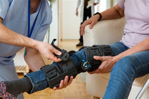 A Male Nurse Helps To Put A Bondage Medical Splint Knee Brace On The Leg Of An Elderly Female