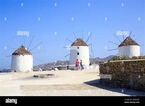 The Famous Windmills Of Mykonos Located On A Hill Just Over The Old Town With Tourists And A