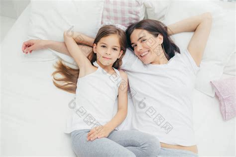 室内拍摄的欢快的母亲和女儿抱着躺在白色被图片 包图网企业站