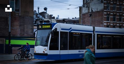 고층 건물 옆 거리를 따라 이동하는 파란색과 흰색 기차 사진 Unsplash의 무료 암스테르담 이미지