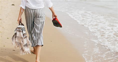 세련된 힙스터 소녀는 맨발로 해변을 걷고 가방과 신발을 손에 들고 있습니다 행복한 보헤미안 여자는 바다에서 휴식을 취하고 열대 섬에서 산책을 즐기고 있다 여름 방학