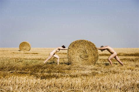 A Naked Man And A Naked Woman Pushing A Hay Bale In The Middle Of A Field Stock Photo