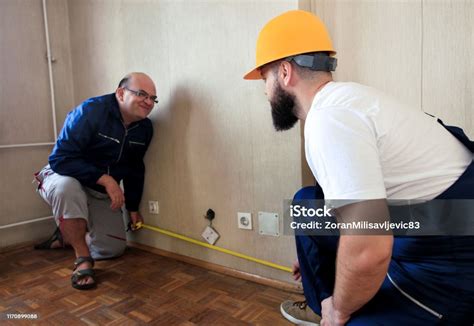 엔지니어 계약자 및 프로젝트 관리자는 동료 건설 노동자 핸디맨 및 빌더와 함께 건설 현장에서 측정 테이프를 사용하여 리노베이션을 위해 아파트의 벽실을 측정하고 있습니다 2